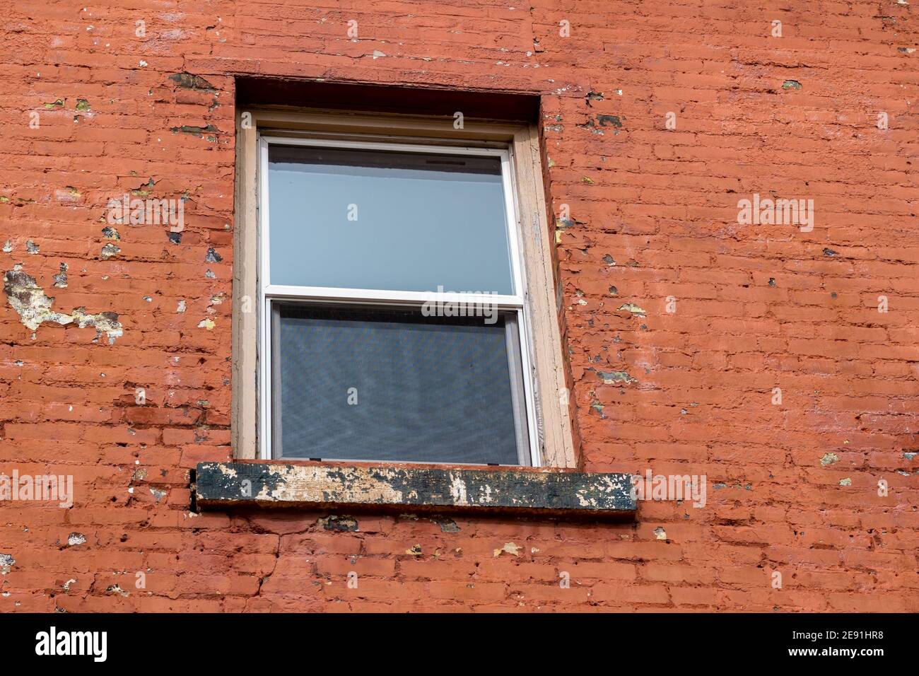 Single window on an old deteriorating rusty red color painted brick ...