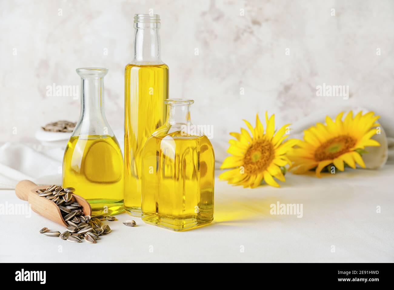 Bottles of oil, scoop with seeds and sunflowers on light background ...