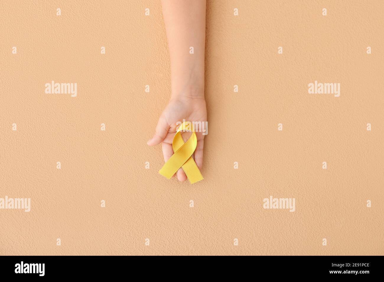 Child's hand with golden ribbon on color background. Cancer awareness ...