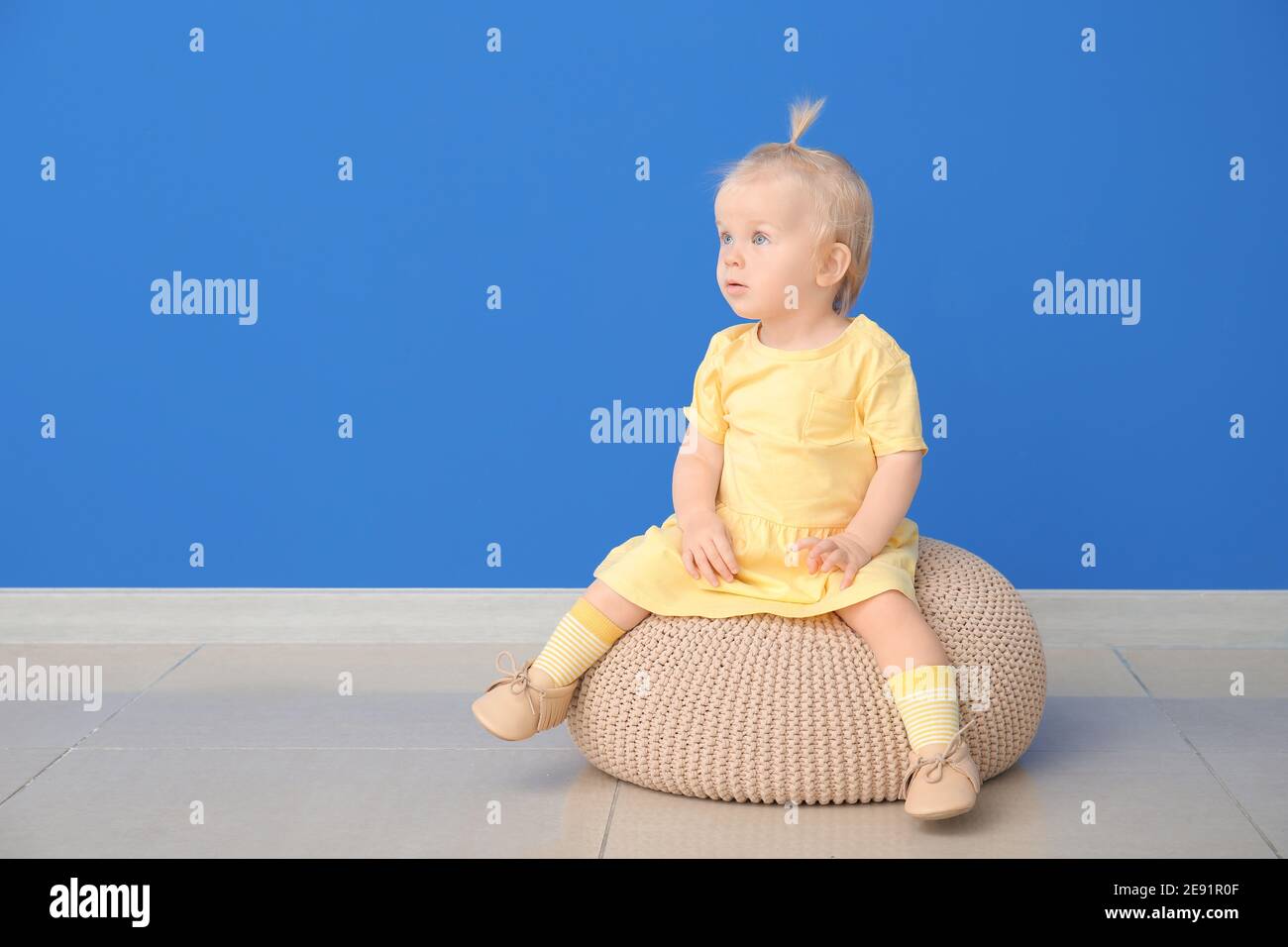 Portrait of cute little baby girl sitting on pouf near color wall Stock ...