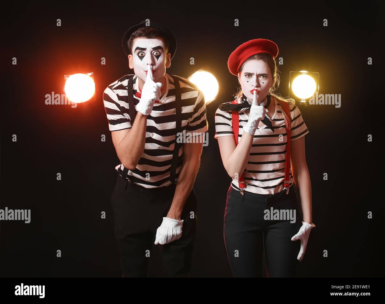 Male and female pantomimists showing silence gesture on dark background ...