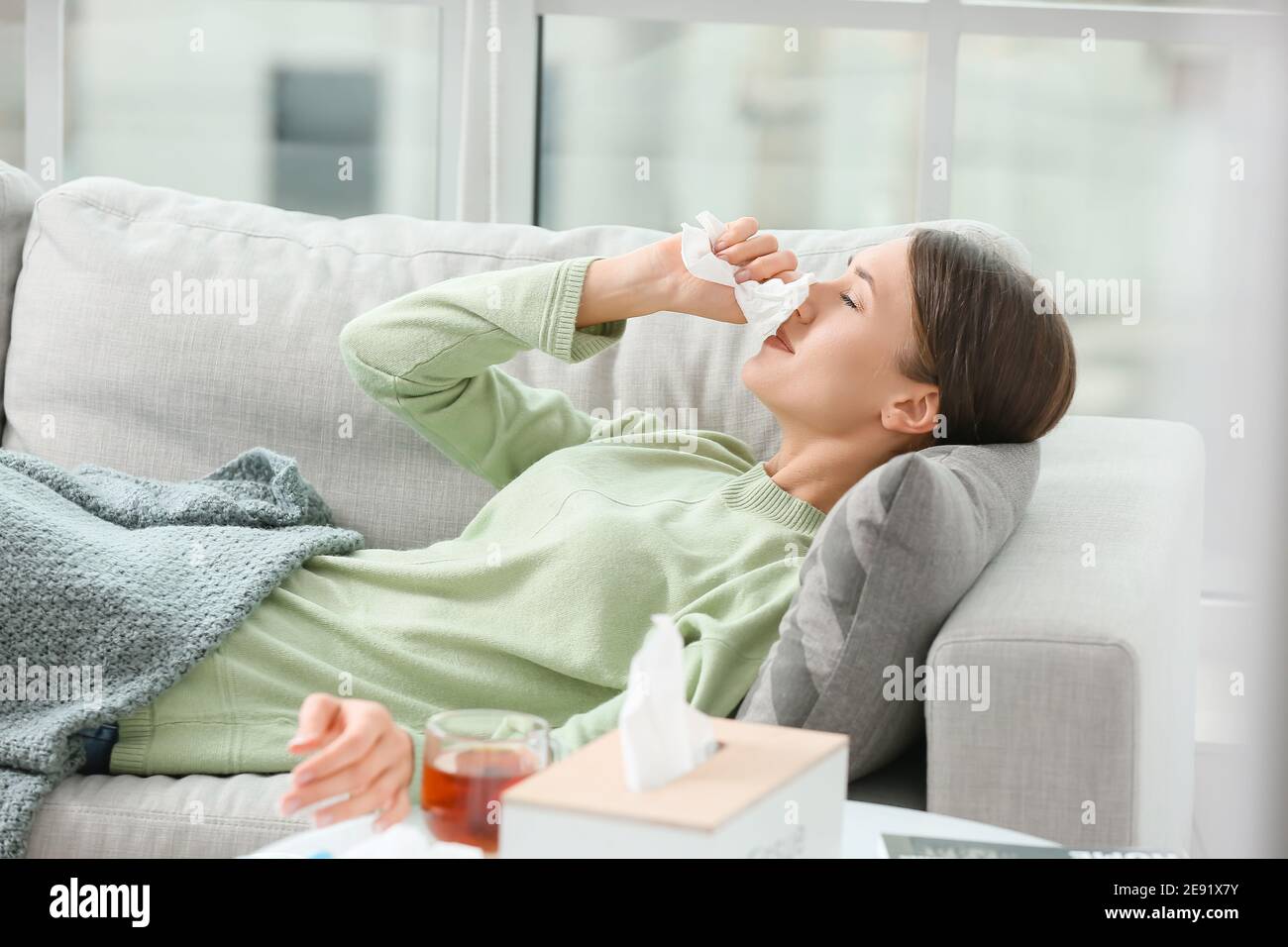 Sick young woman lying on sofa at home Stock Photo - Alamy