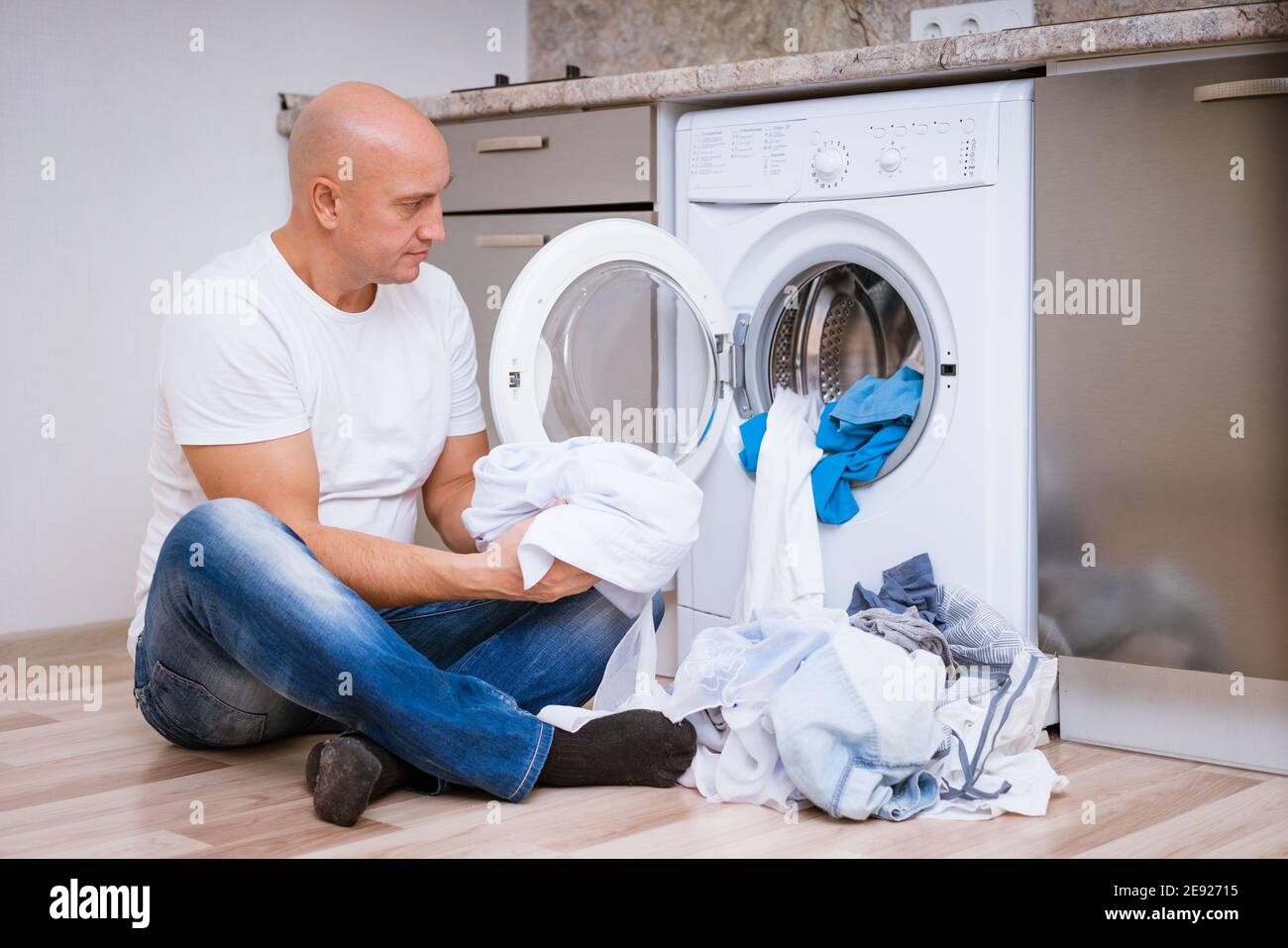 tired bald man sitting with dirty laundry in the washing machine ...