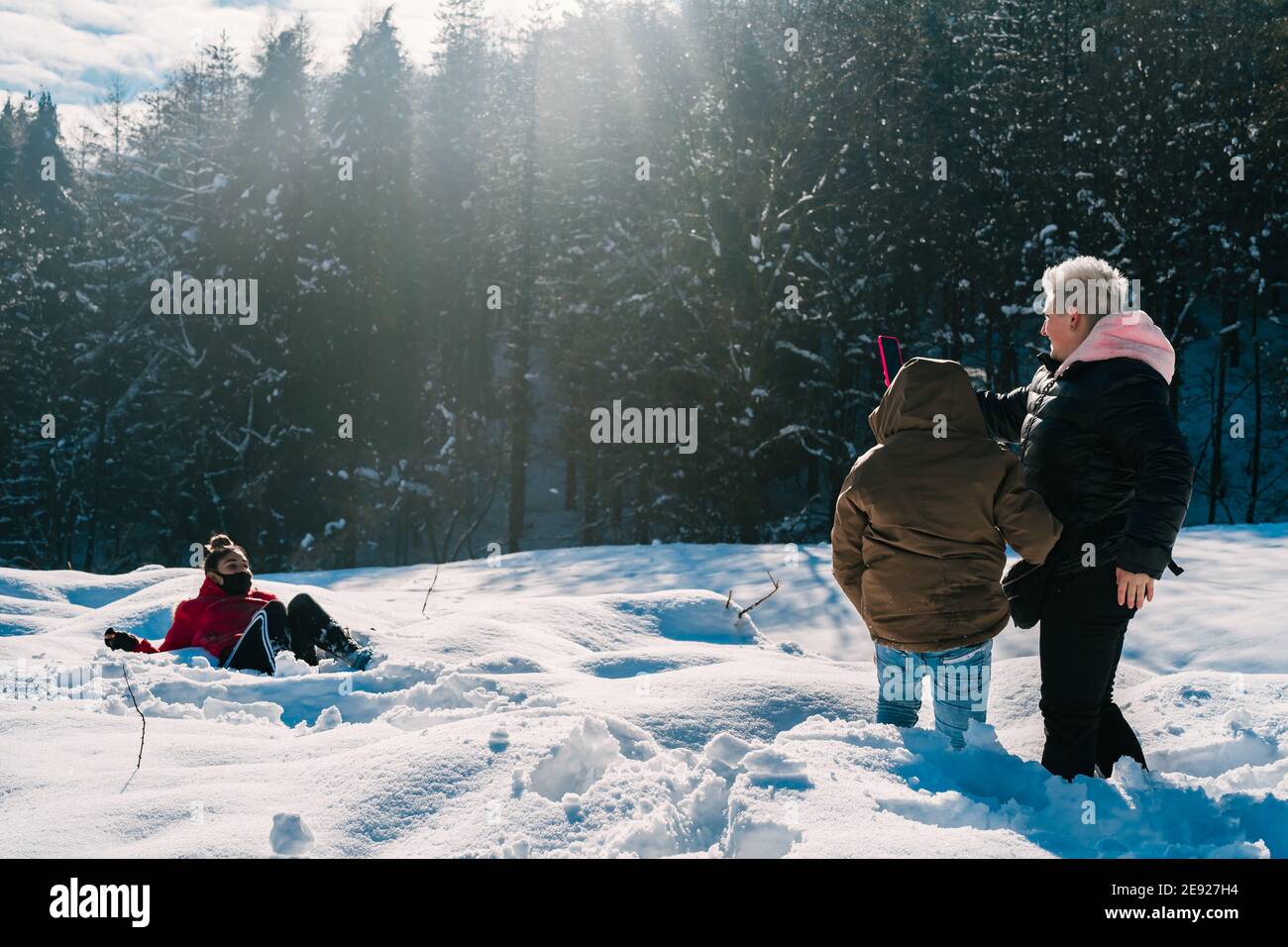 Young happy mother taking a photo of her teen daughter fallen on snow ...