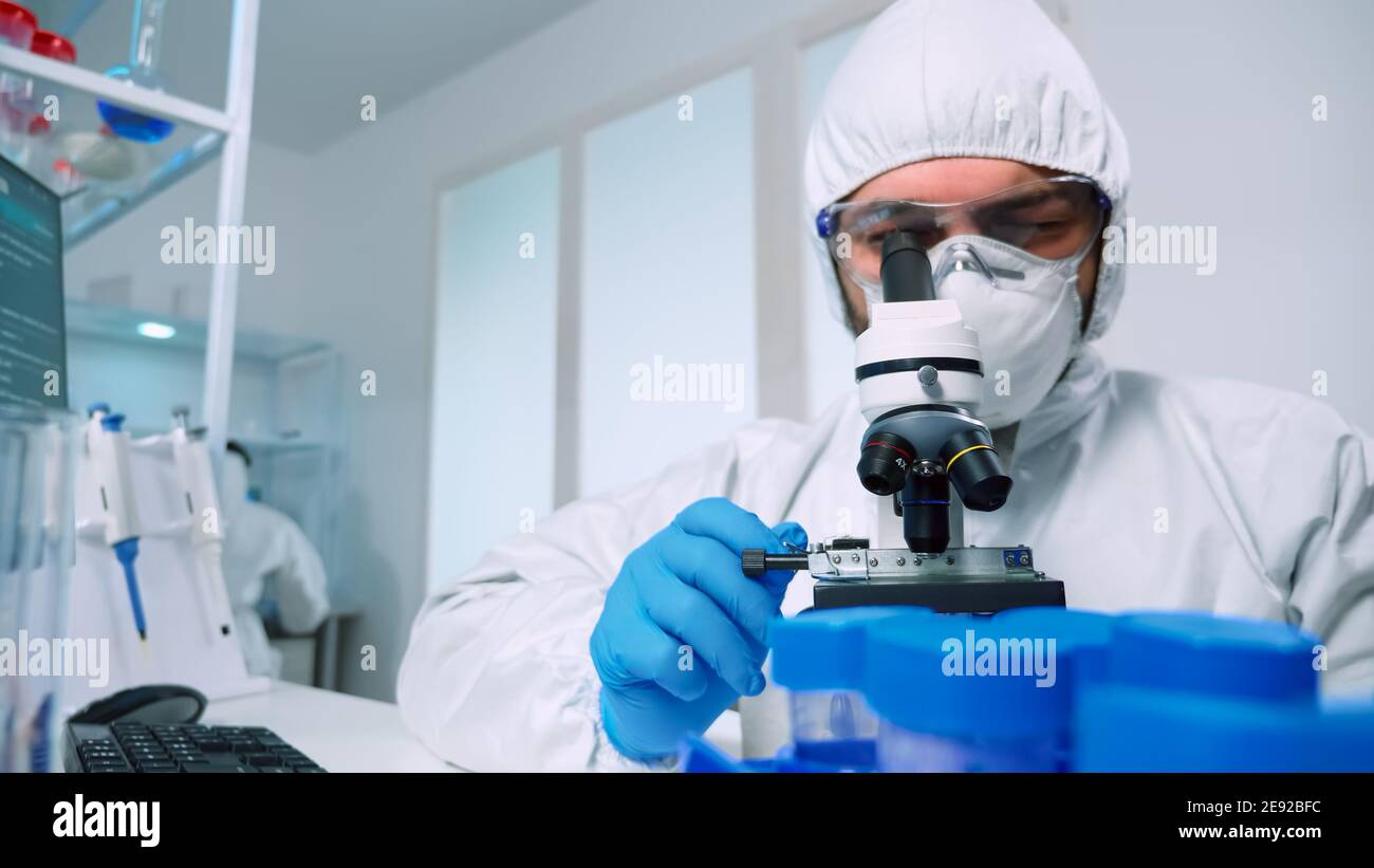 Laboratory scientist in ppe suit conducting experiment looking through ...