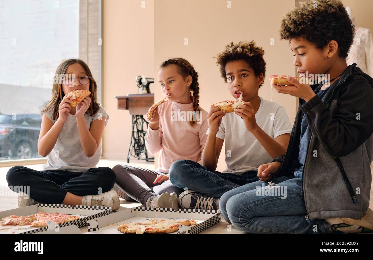 Group of hungry multi racial kids little boys girls sit indoor eating ...