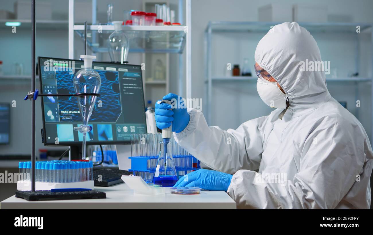 Chemist wearing ppe suit putting liquid in test tube with micropipette ...