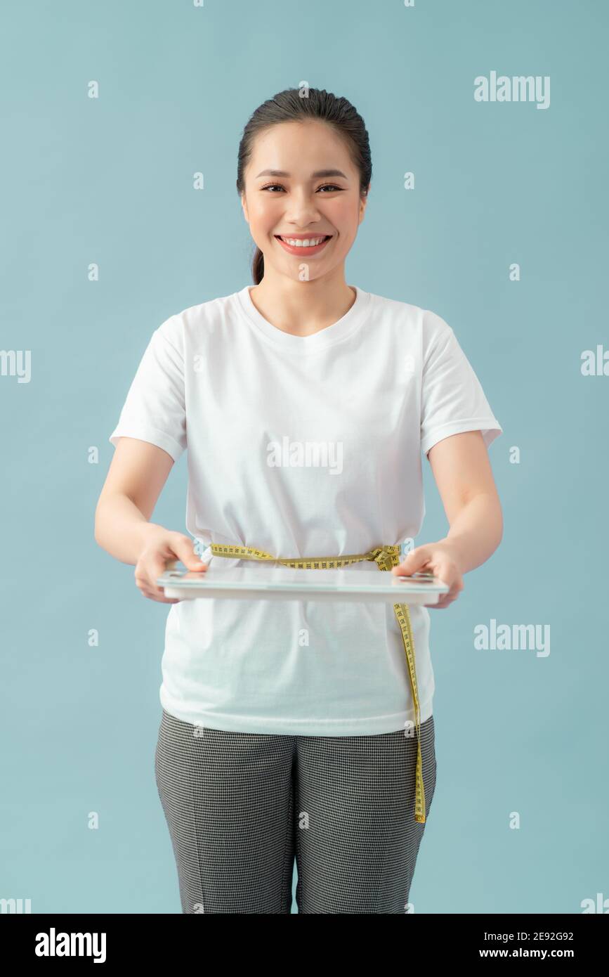 A asian woman holding scales with a tape measure around her belly on a ...