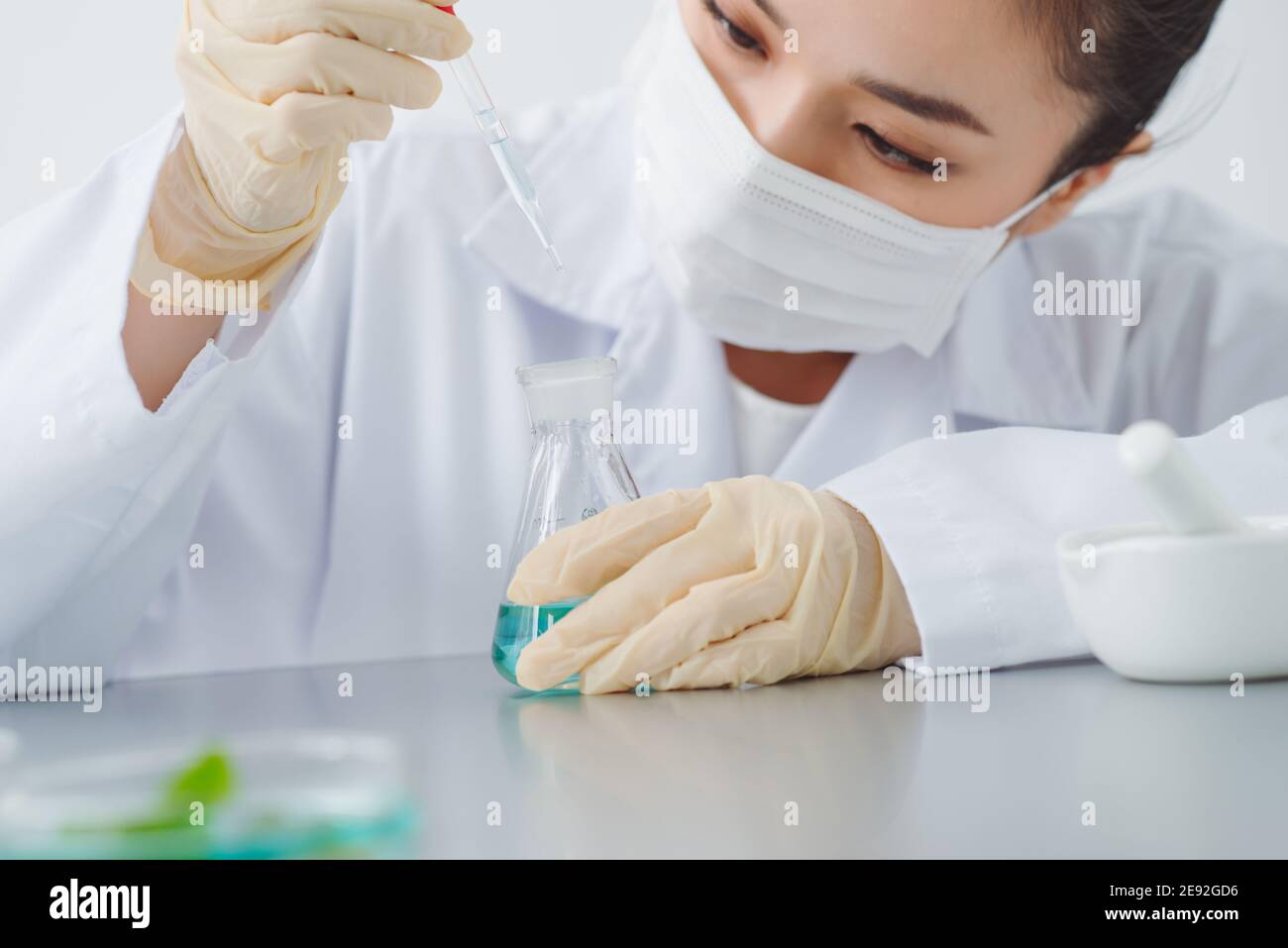Lab worker dripping water into flask with leaf on blurred background ...