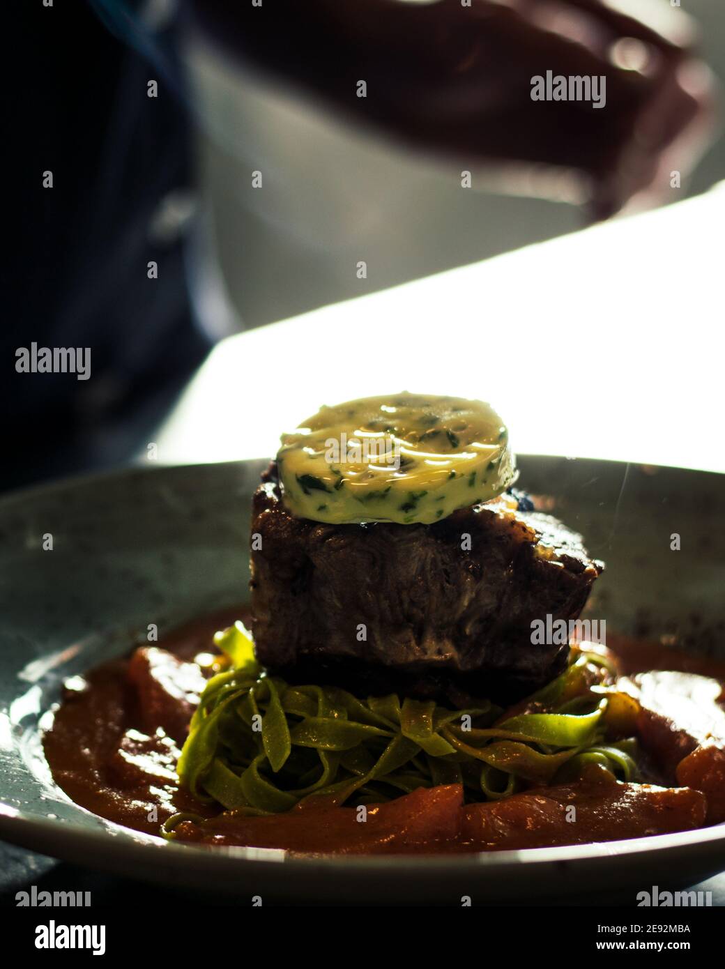 Grilled and flamed ox steak with green herb noodles in a tomato puree ...