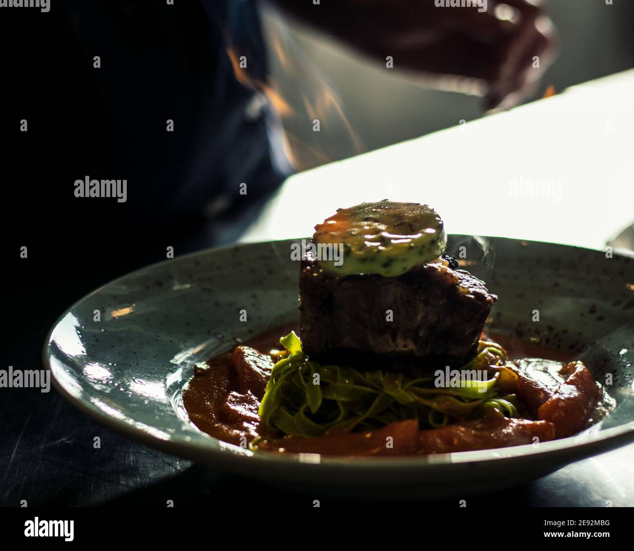 Grilled and flamed ox steak with green herb noodles in a tomato puree ...