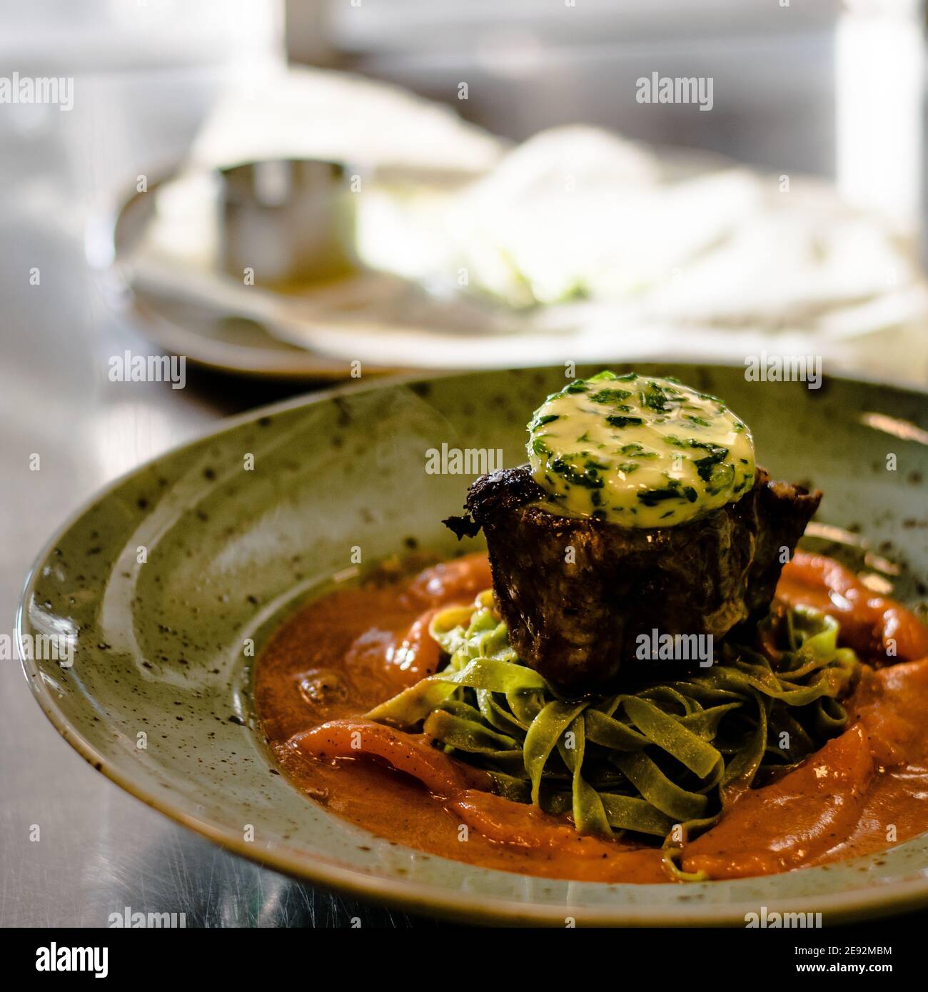 Grilled and flamed ox steak with green herb noodles in a tomato puree ...