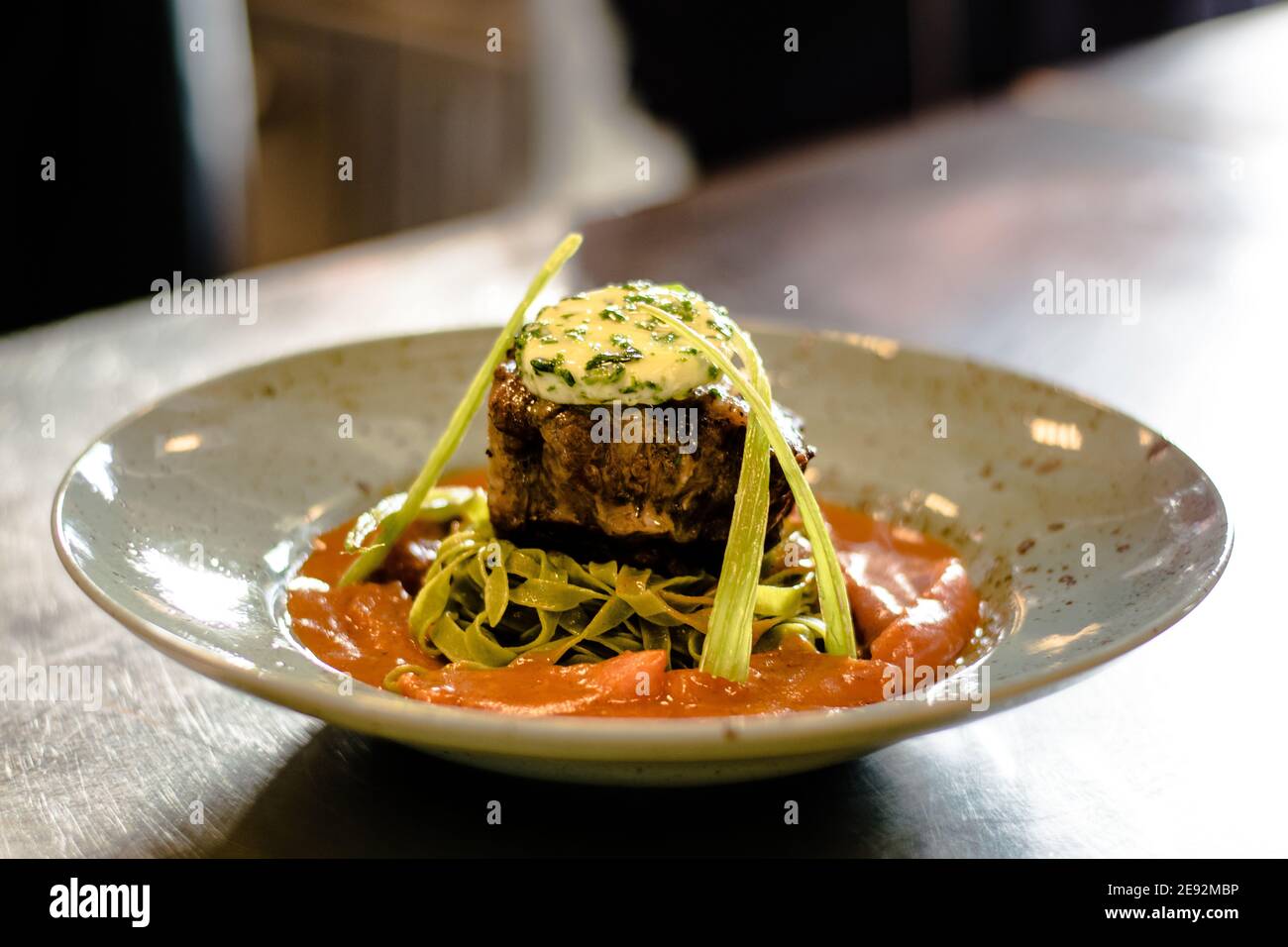 Grilled and flamed ox steak with green herb noodles in a tomato puree ...