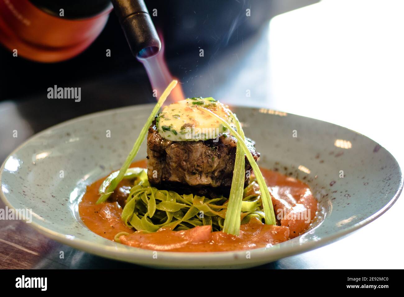 Grilled and flamed ox steak with green herb noodles in a tomato puree ...