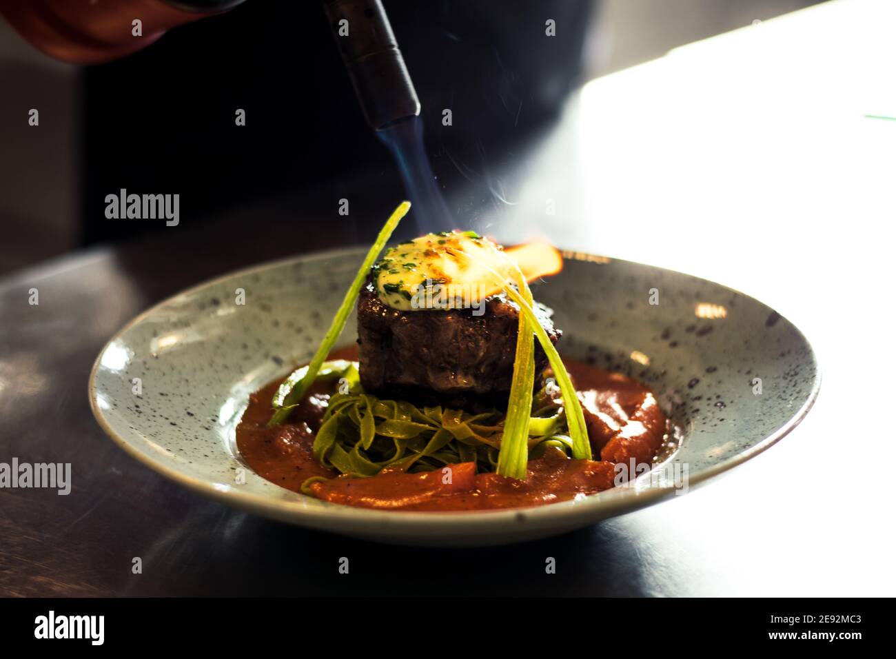 Grilled and flamed ox steak with green herb noodles in a tomato puree ...