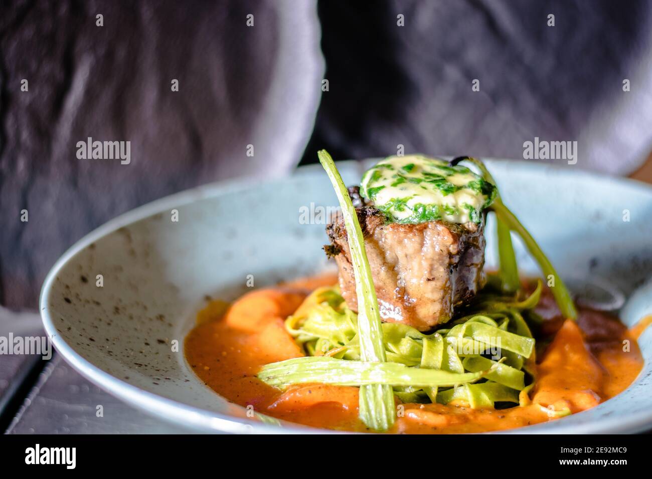 Grilled and flamed ox steak with green herb noodles in a tomato puree ...