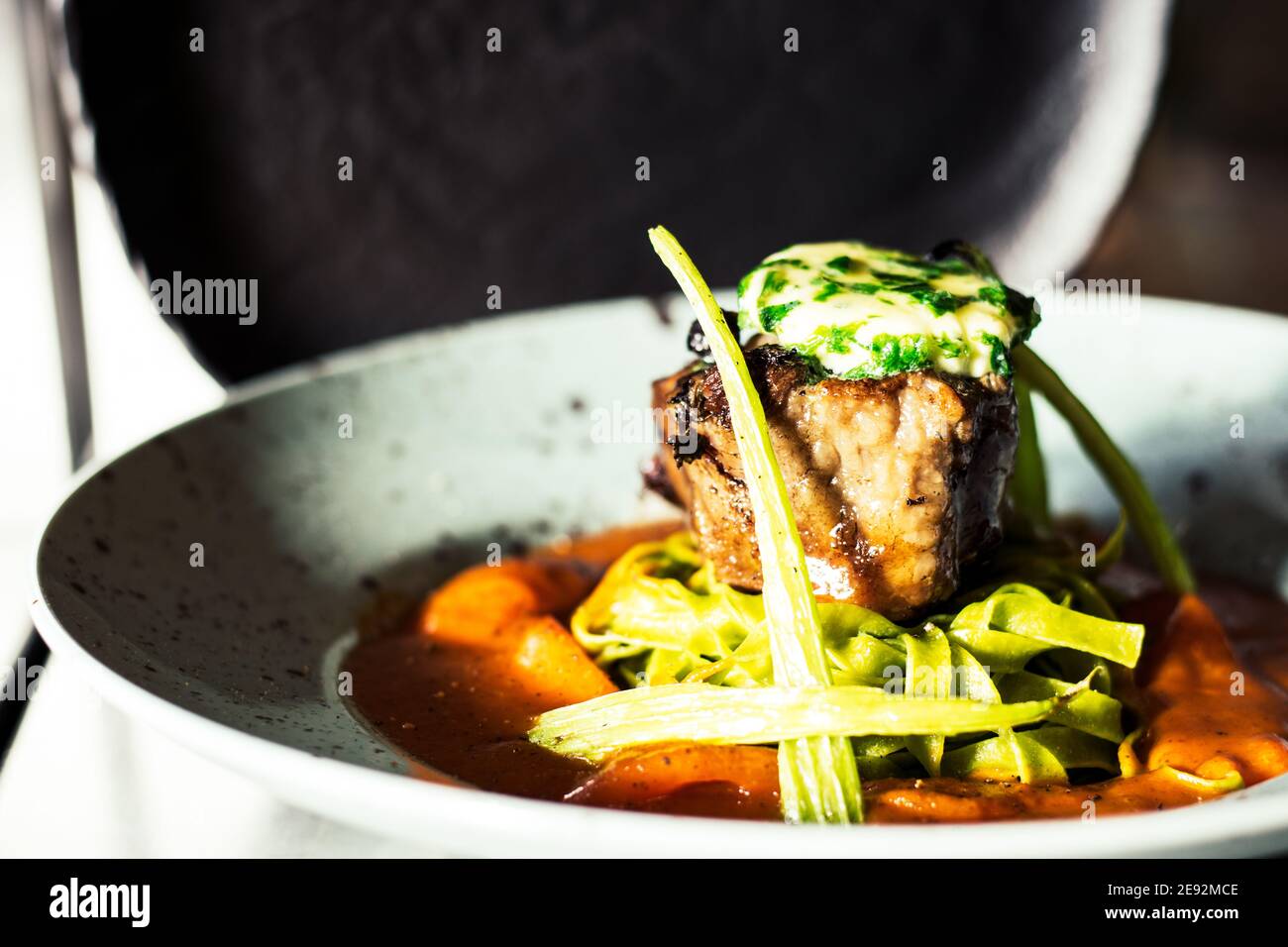 Grilled and flamed ox steak with green herb noodles in a tomato puree ...