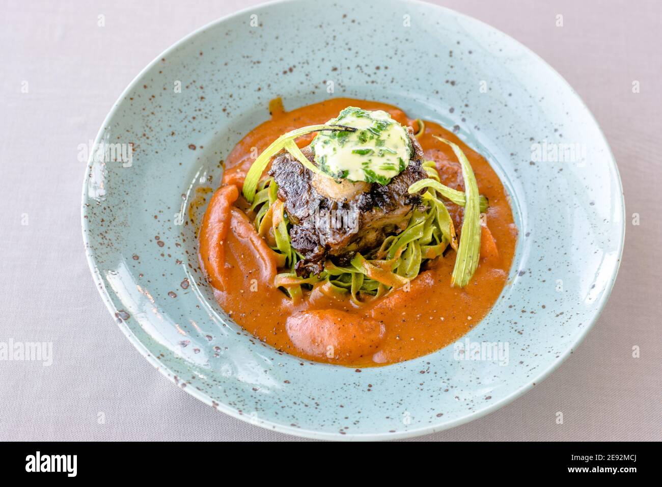 Grilled and flamed ox steak with green herb noodles in a tomato puree ...