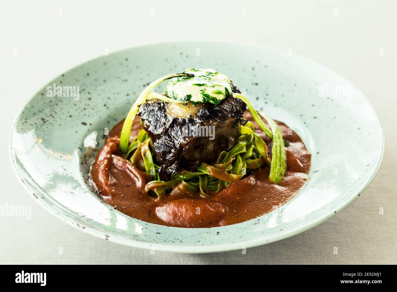 Grilled and flamed ox steak with green herb noodles in a tomato puree ...