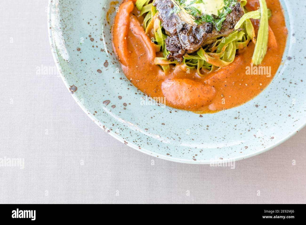 Grilled and flamed ox steak with green herb noodles in a tomato puree ...