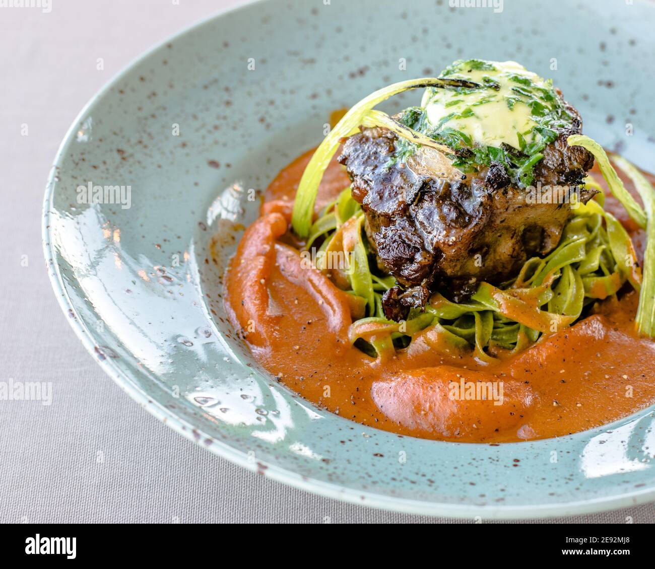 Grilled and flamed ox steak with green herb noodles in a tomato puree ...