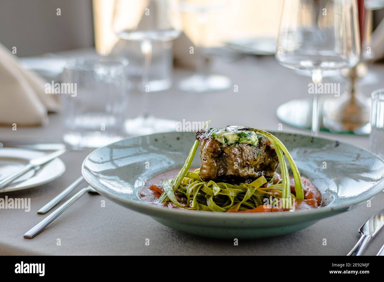 Grilled and flamed ox steak with green herb noodles in a tomato puree ...