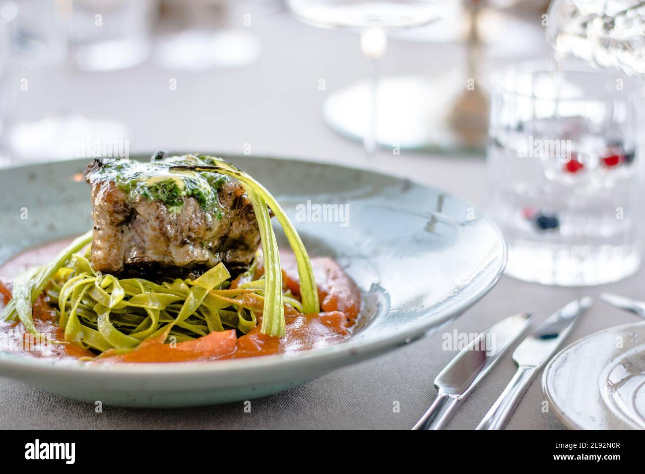 Grilled and flamed ox steak with green herb noodles in a tomato puree ...