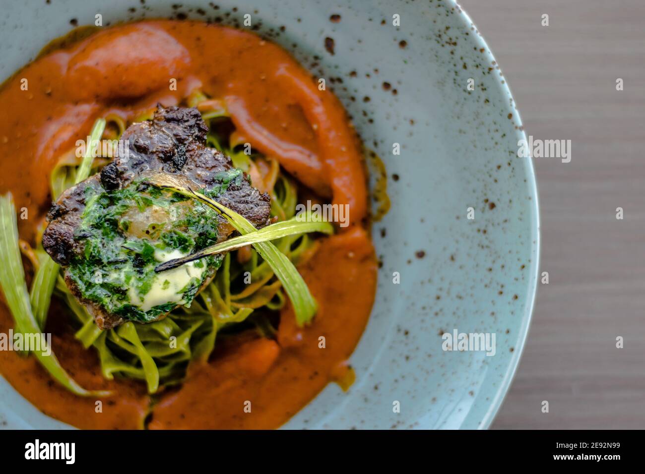 Grilled and flamed ox steak with green herb noodles in a tomato puree ...