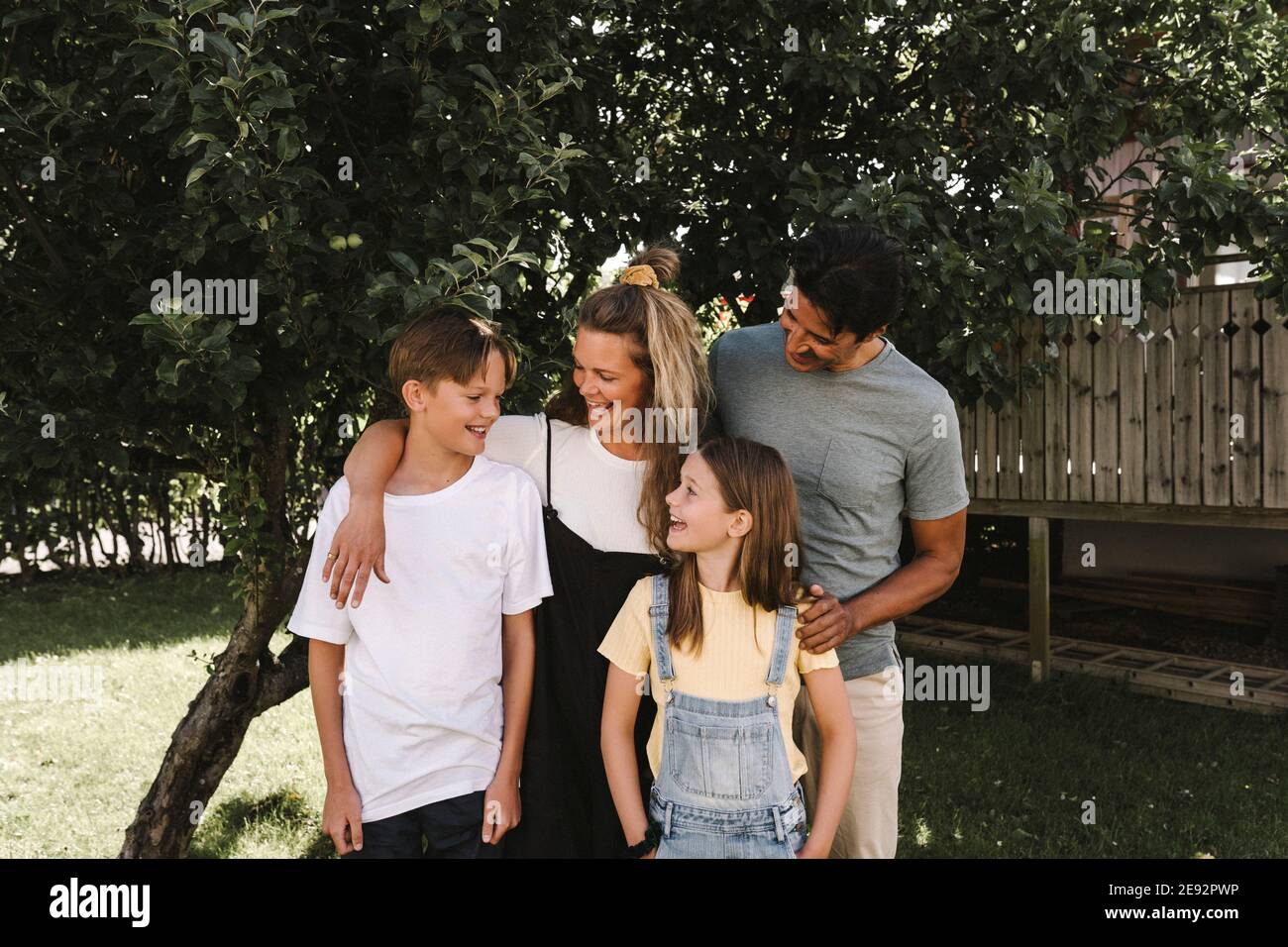 Smiling parents with children against tree in front yard Stock Photo ...