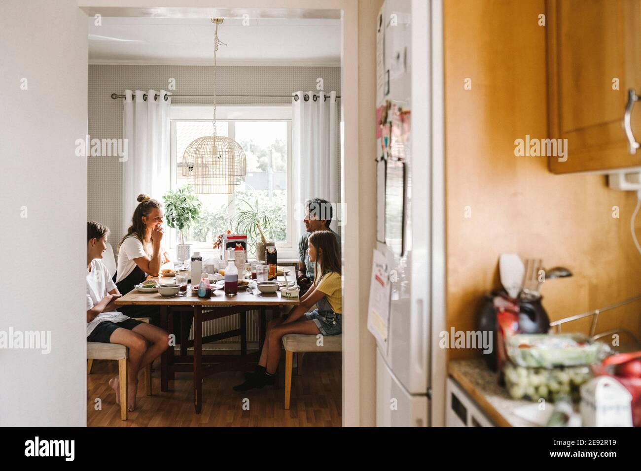 Happy family eating breakfast seen through doorway of kitchen at home ...