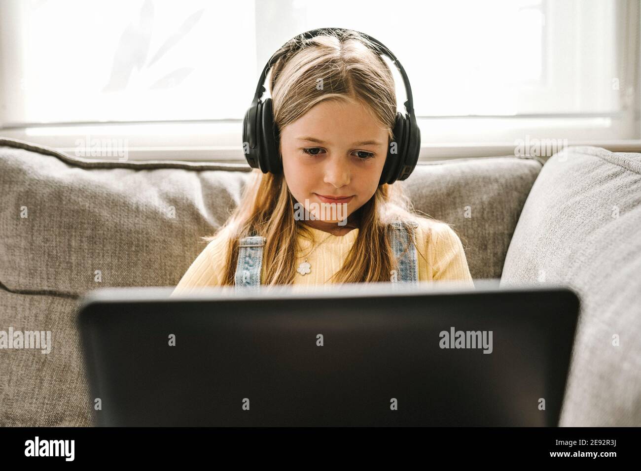 Pre-adolescent girl concentrating while e-learning on laptop in living ...
