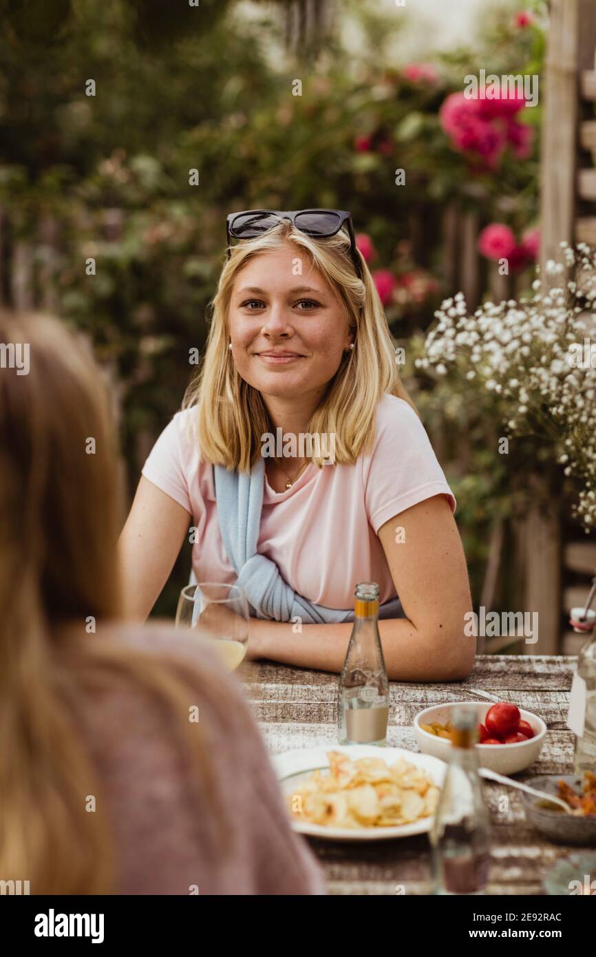 Smiling teenage girl sitting with food at table during dinner party ...