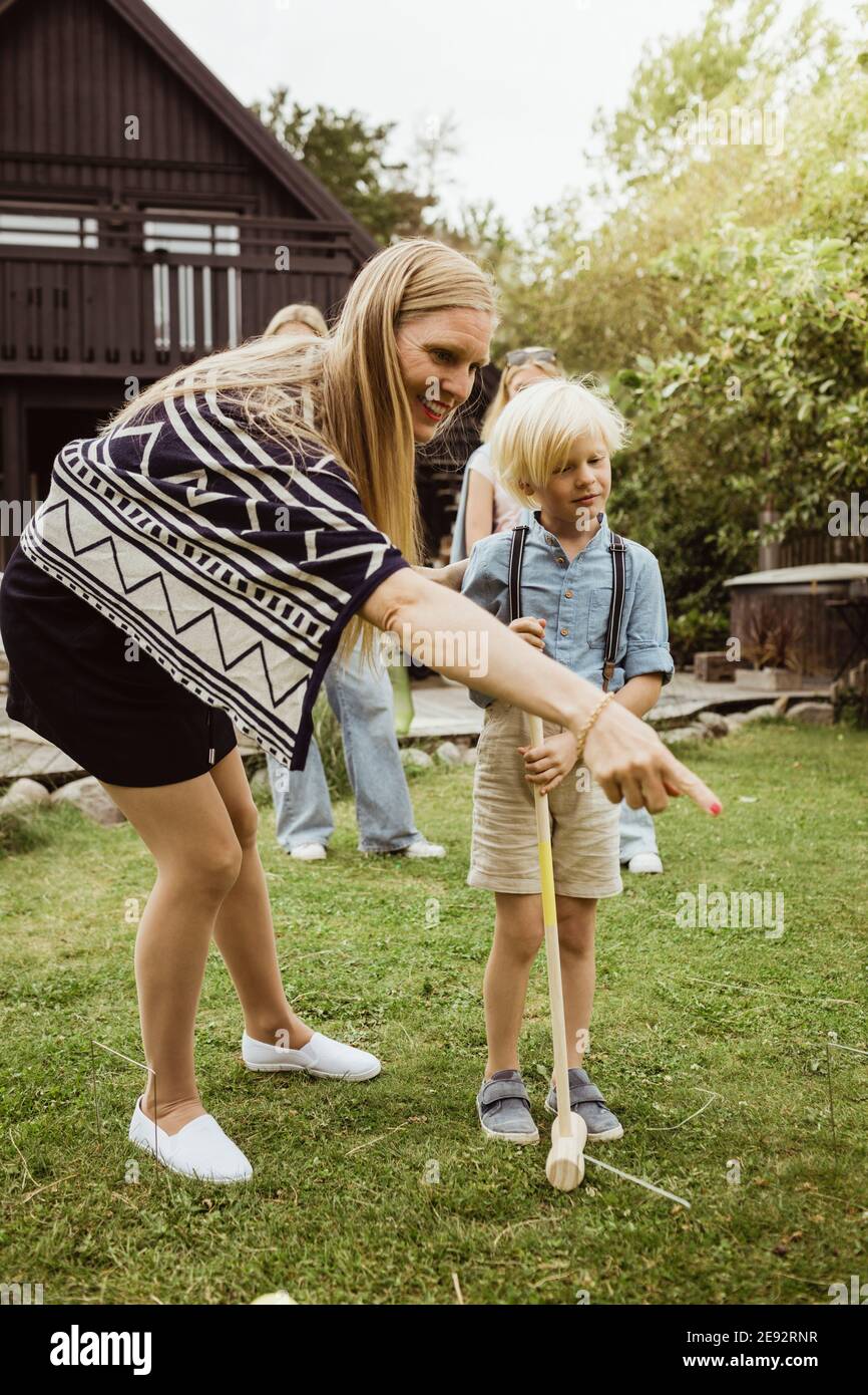 Mother pointing while standing by son playing polo in front yard Stock ...