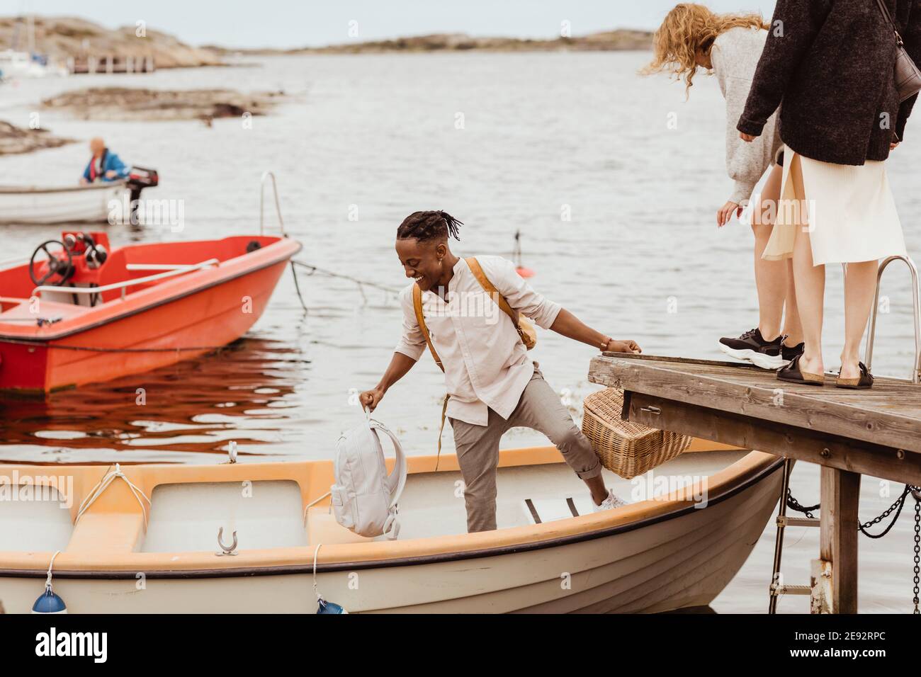 Smiling man helping female friends boarding boat by harbor Stock Photo ...