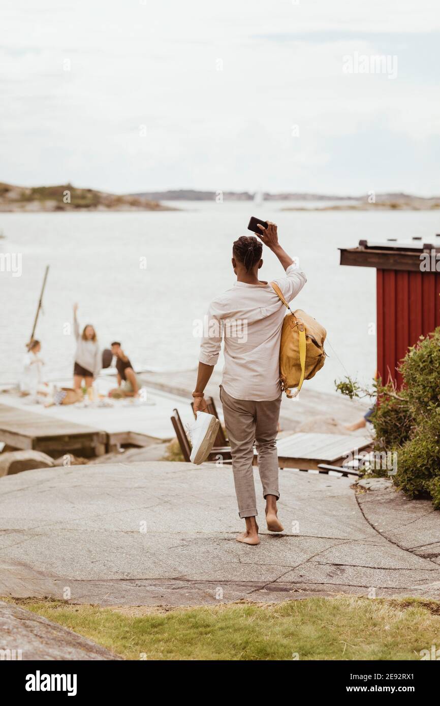 Rear view of man waving at friends sitting on jetty during picnic at ...