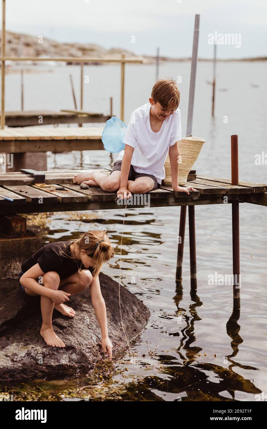 Siblings fishing by jetty at sea during vacation Stock Photo - Alamy