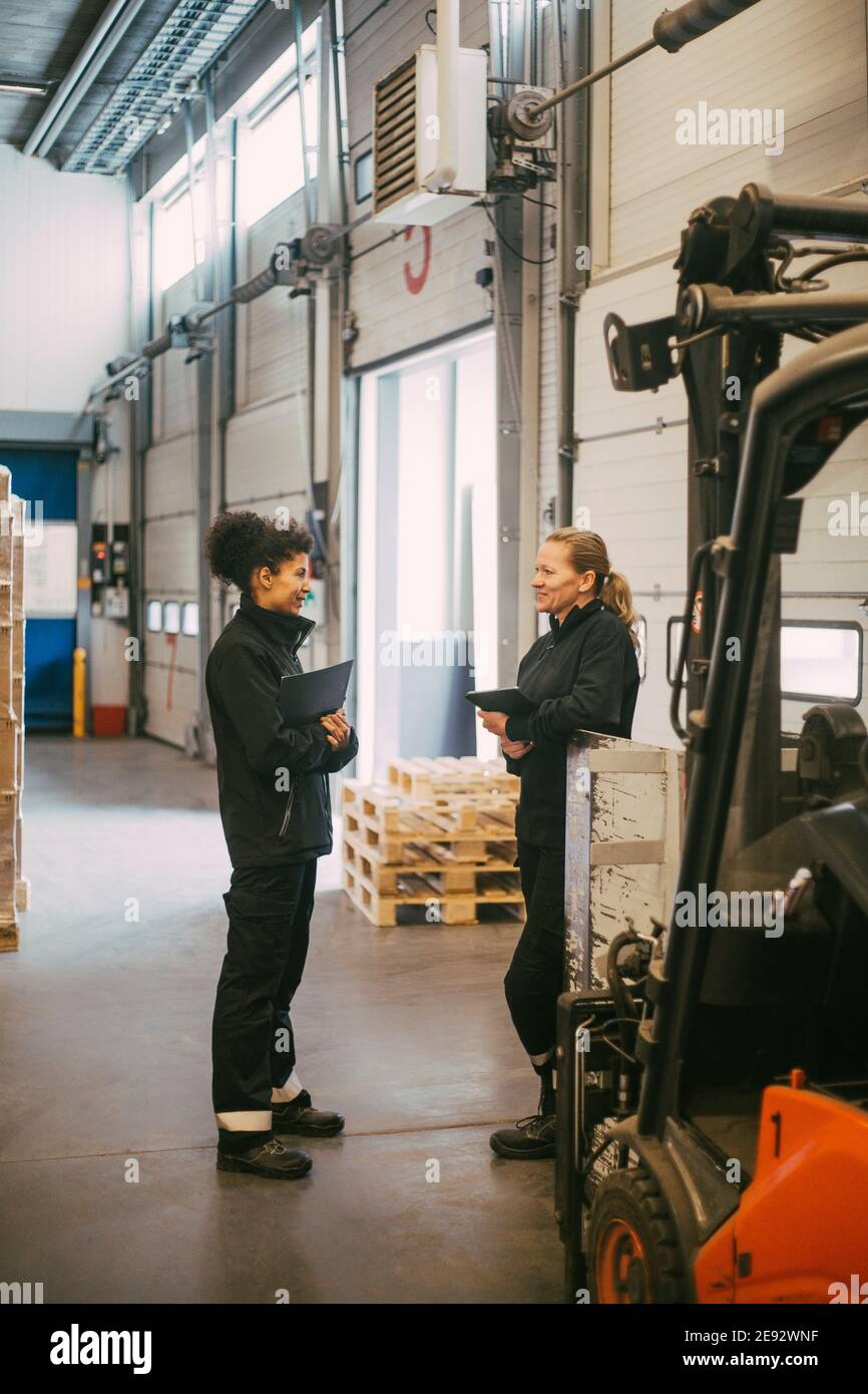 Female manual workers discussing while standing in distribution ...