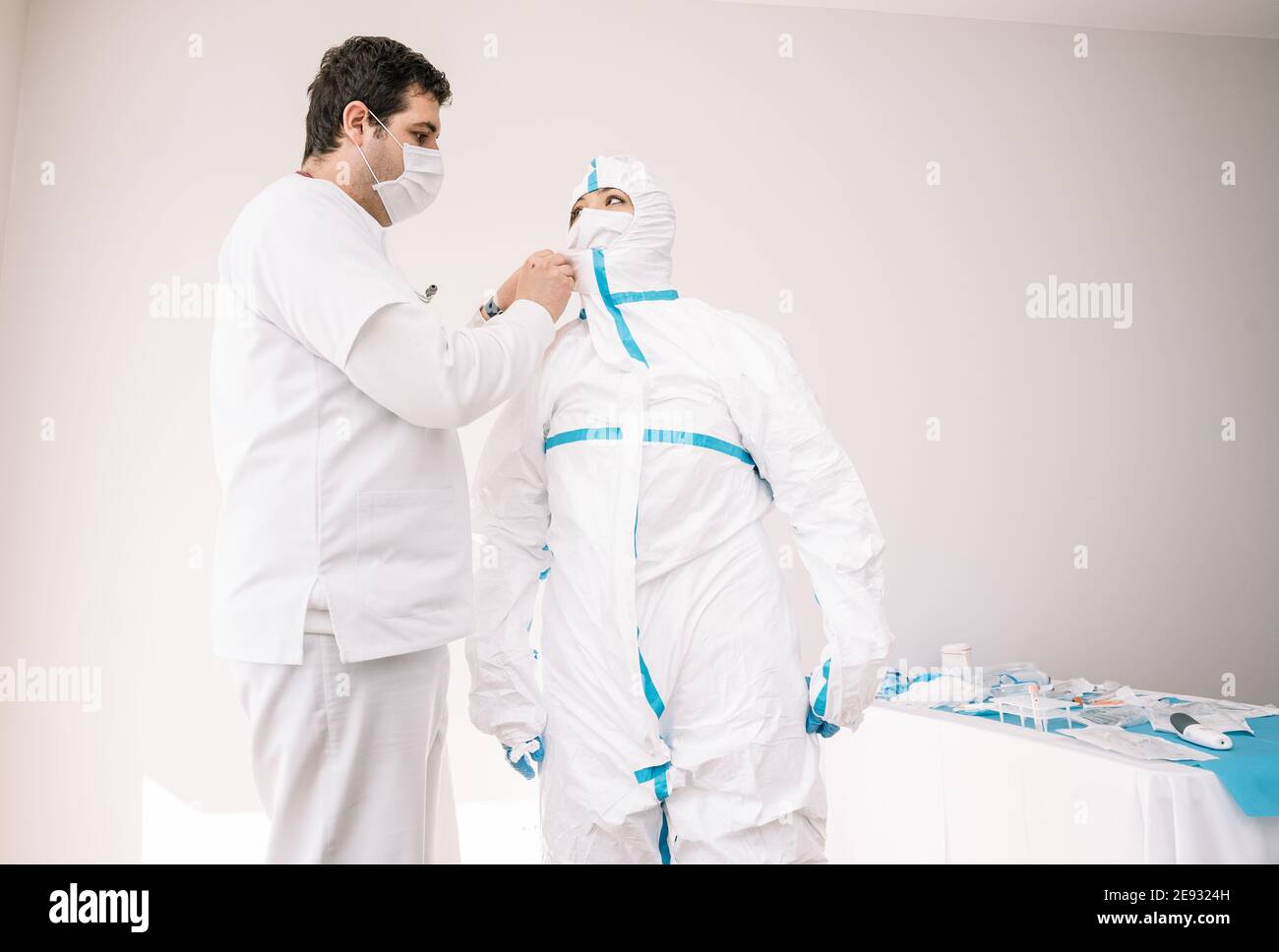 Medic in mask putting on protective costume with help of male coworker ...