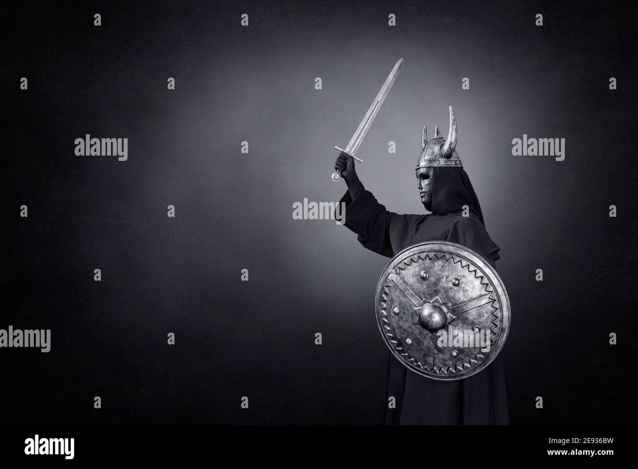Scary figure with horned helmet, sword and round shield in the dark ...
