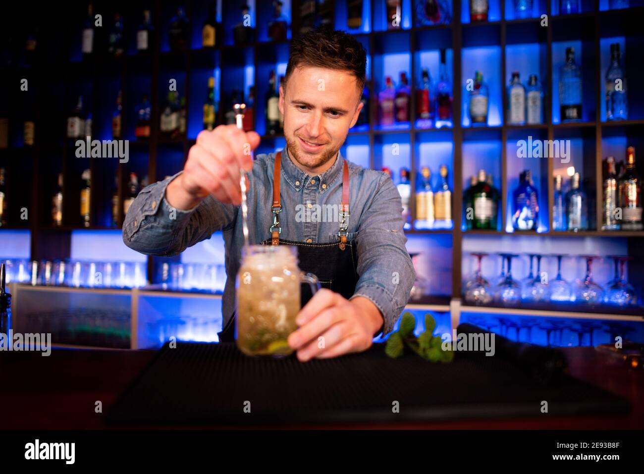 Young guy a working as a bartender while preparing cocktails in a pub ...