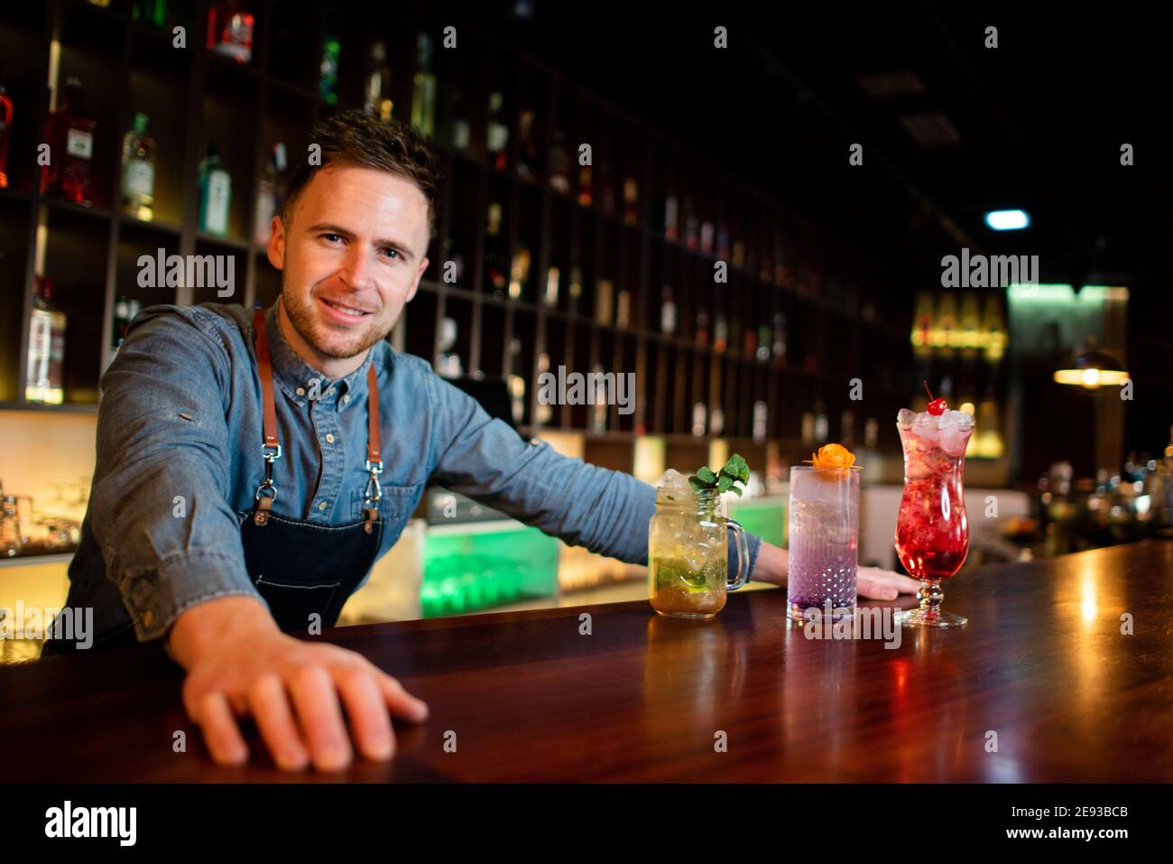 Young guy a working as a bartender while preparing cocktails in a pub ...