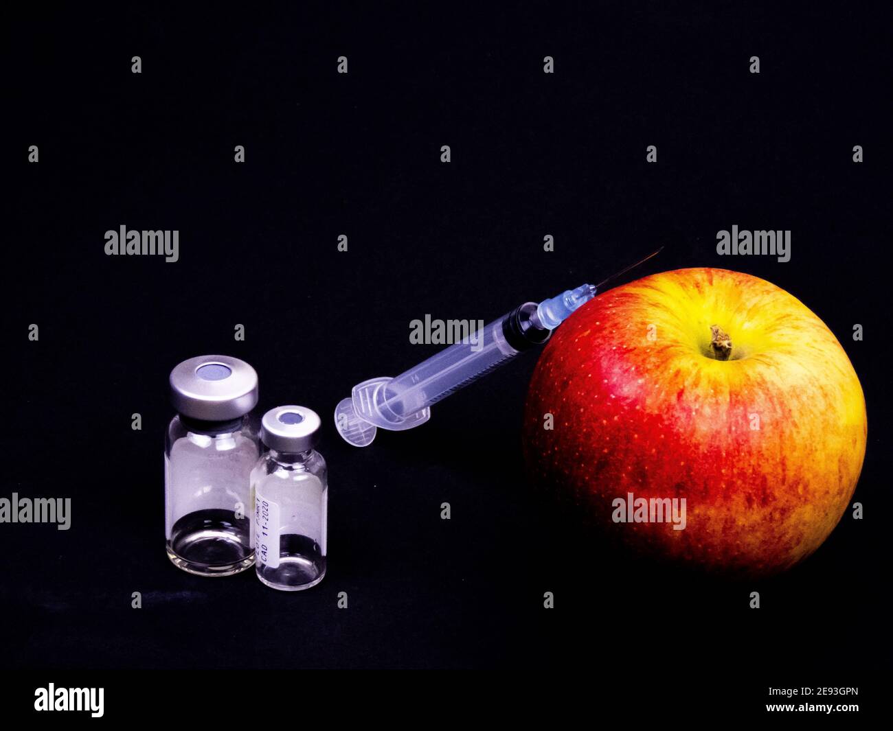 Ripe apple, vials with chemicals, and a syringe isolated in the black ...