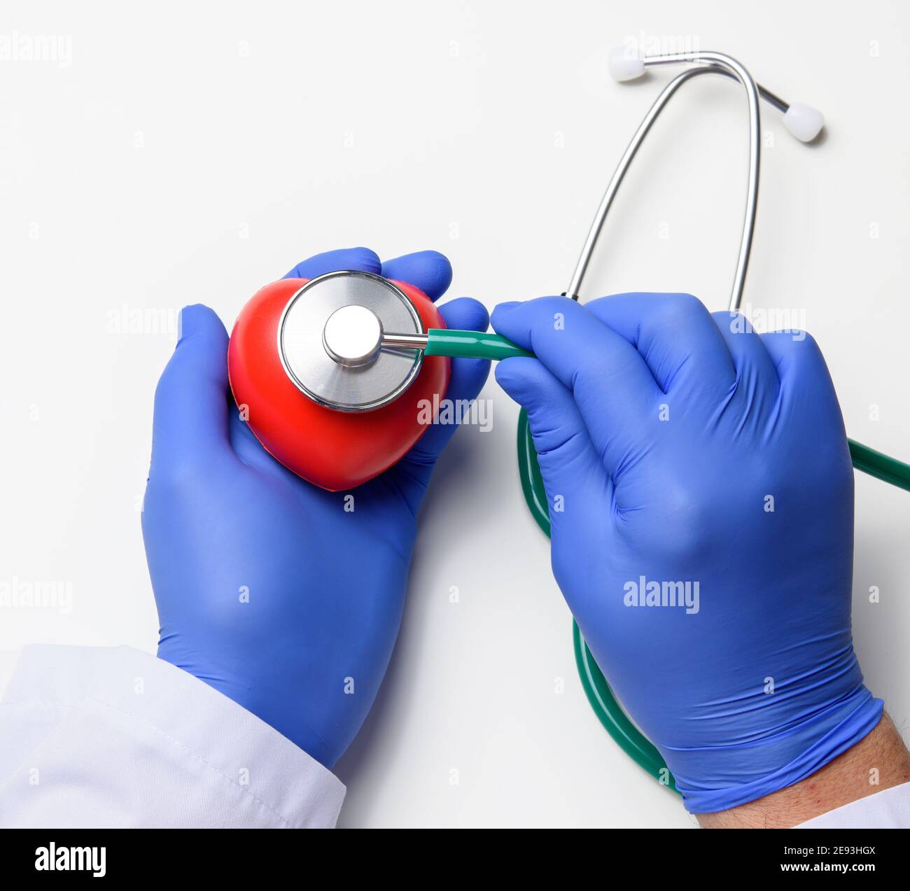 two hands hold medical stethoscope and red rubber heart on white ...