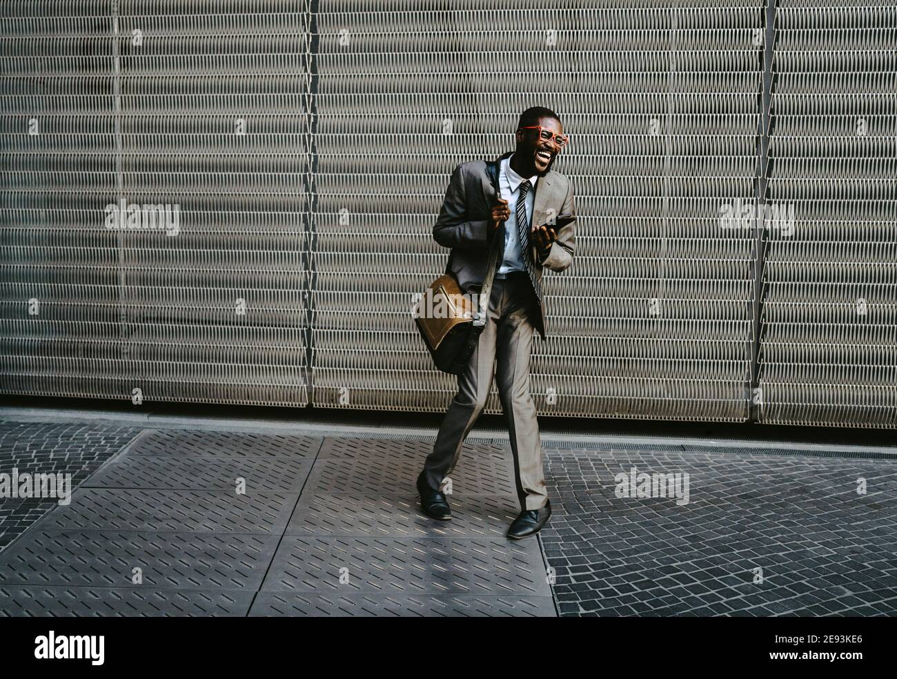 Businessman laughing while standing with smart phone on walkway against ...