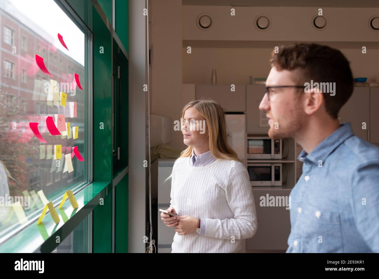 Coworkers looking at notes sticked on window Stock Photo - Alamy