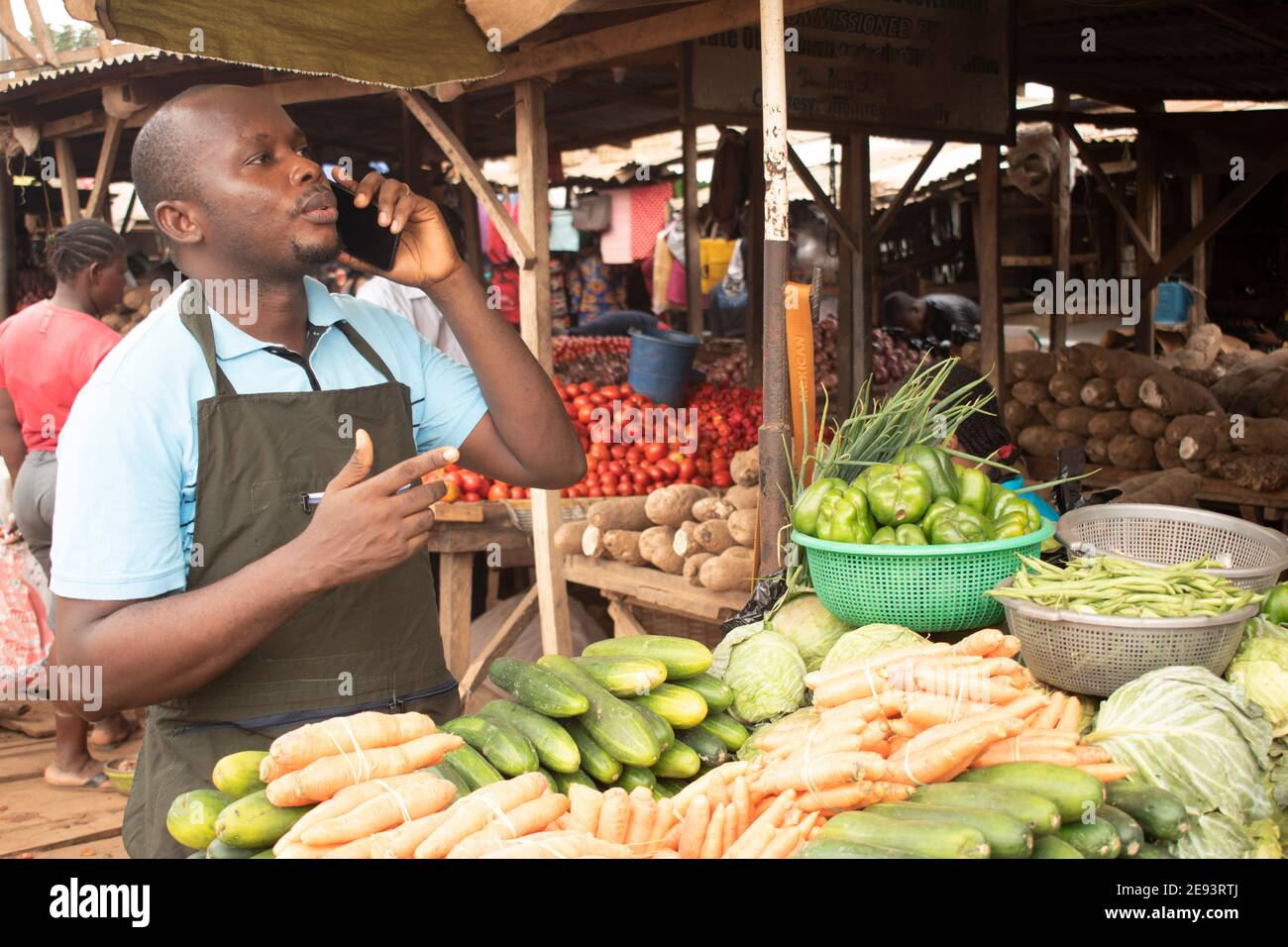 an african market man selling fruits and vegetables making a phone call ...