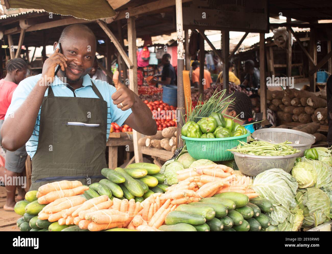 an african market man selling fruits and vegetables making a phone call ...