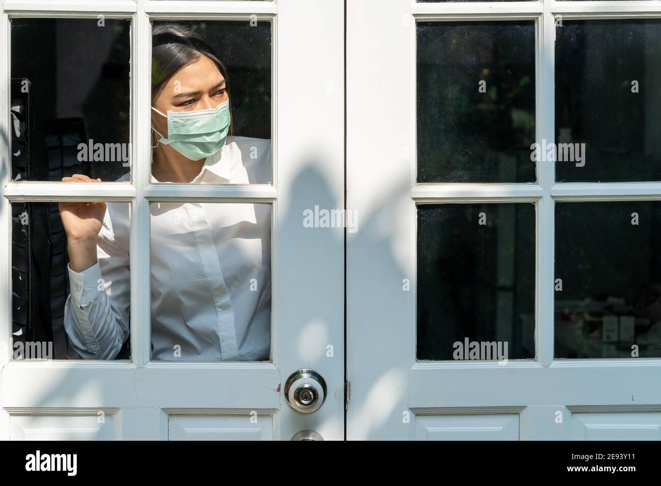 Young woman wearing surgical mask staying inside her home looking out ...