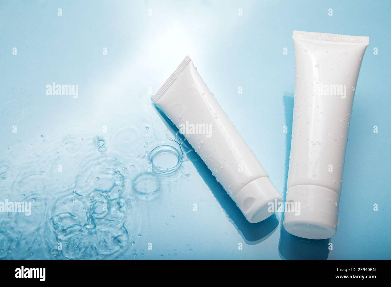 White cosmetic products in tubes on color blue background with water ...