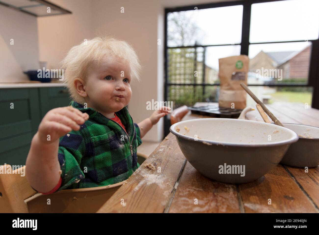 A young child sat at a table with a mixing bowl and baking ingredients ...